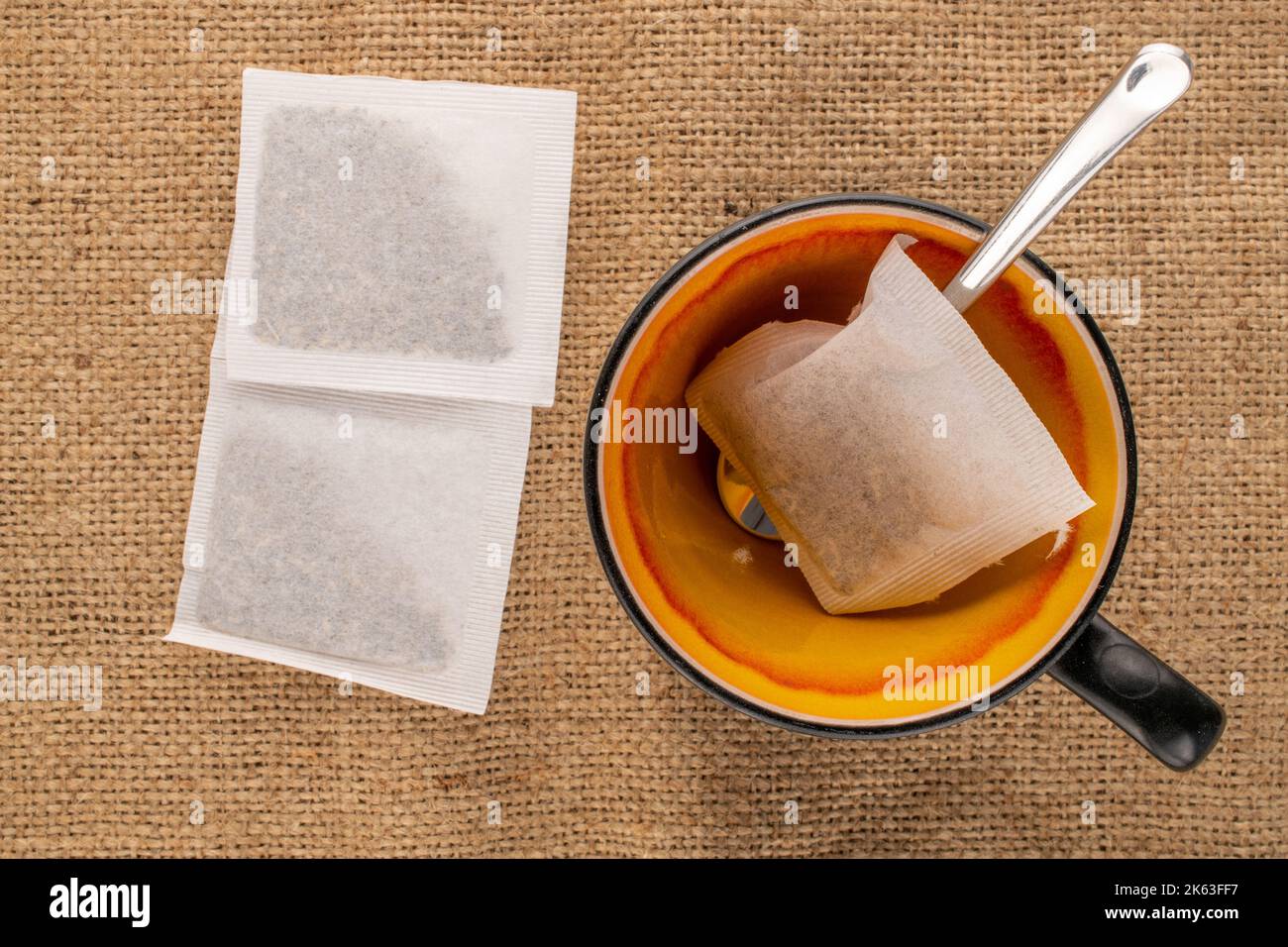 Several aromatic tea bags with black ceramic cup and saucer on jute ...