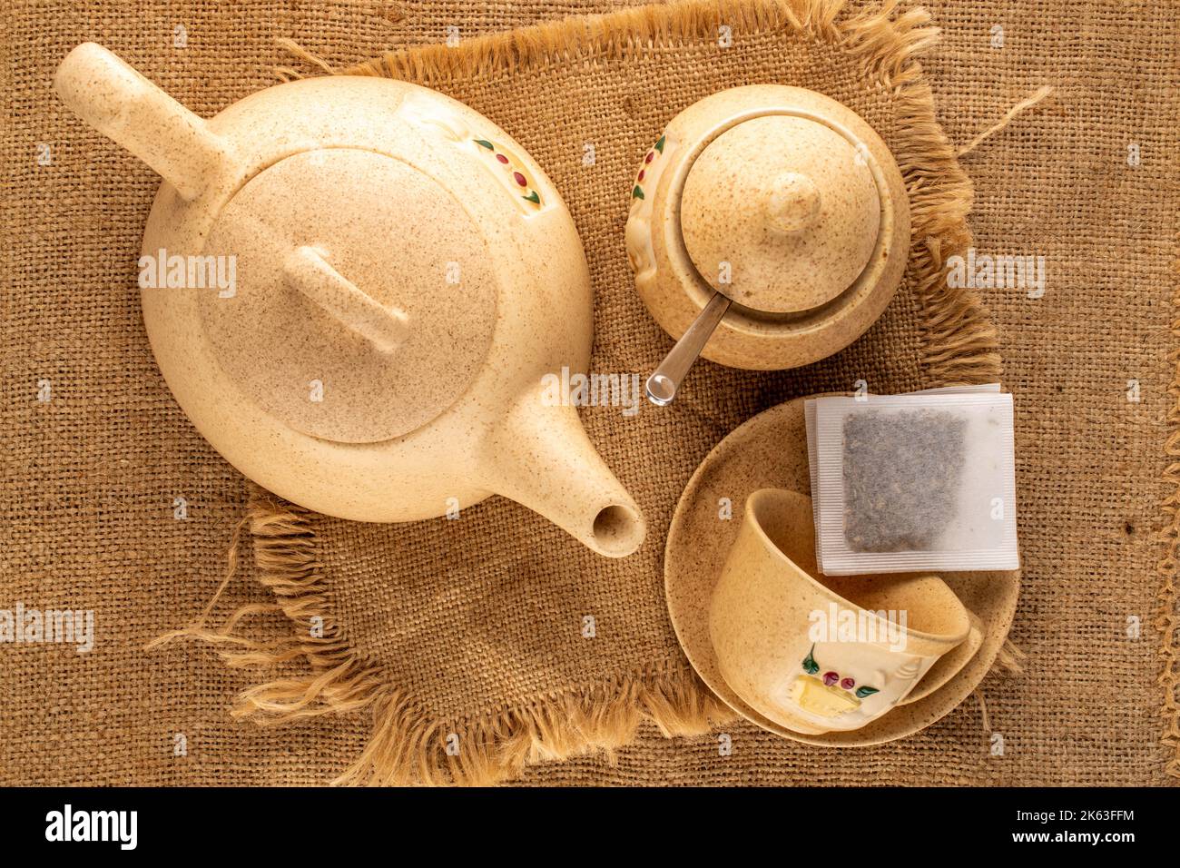 Several aromatic tea bags with ceramic teaware on jute cloth, macro ...