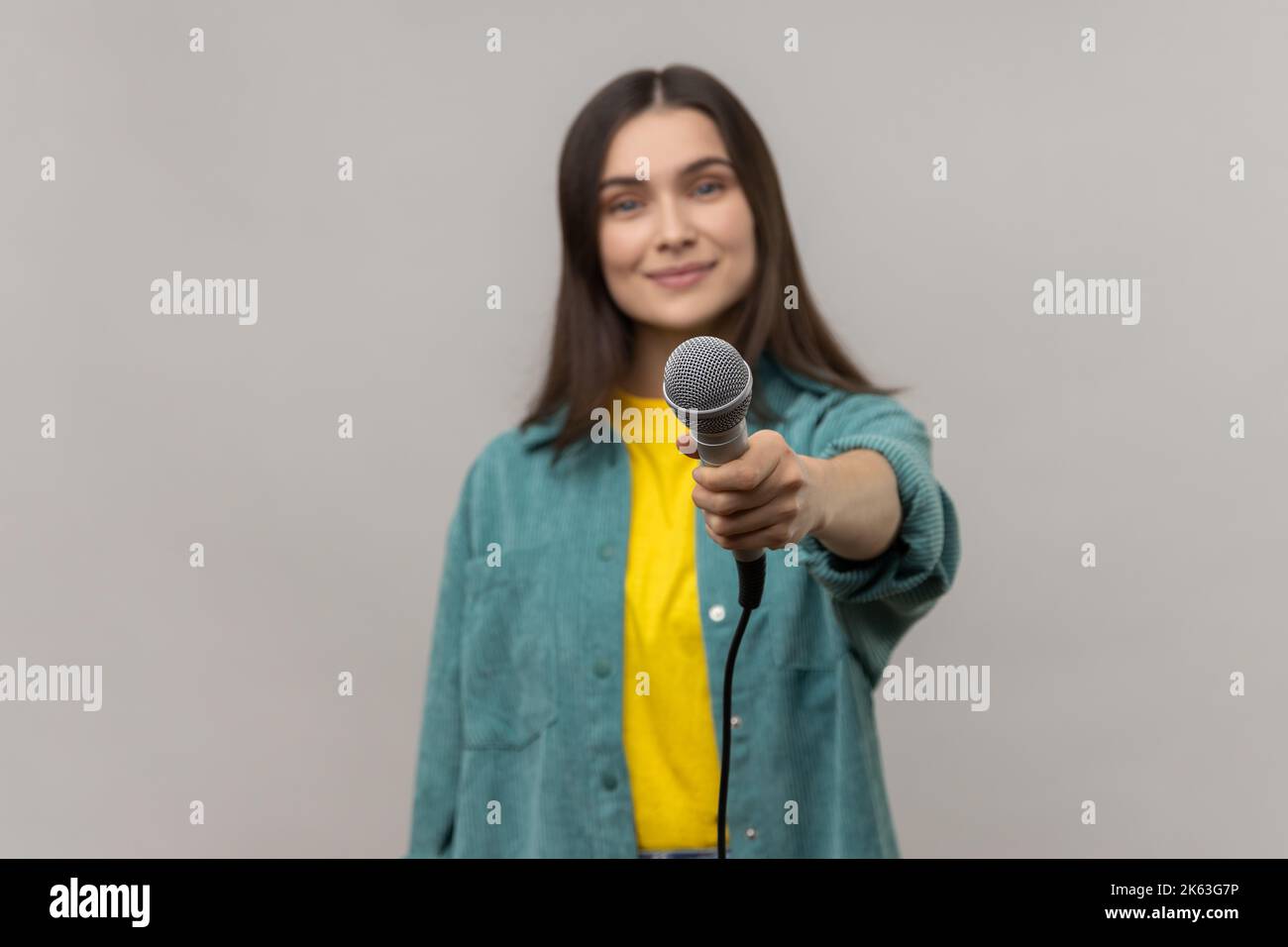 Portrait of satisfied woman with dark hair standing offering microphone ...