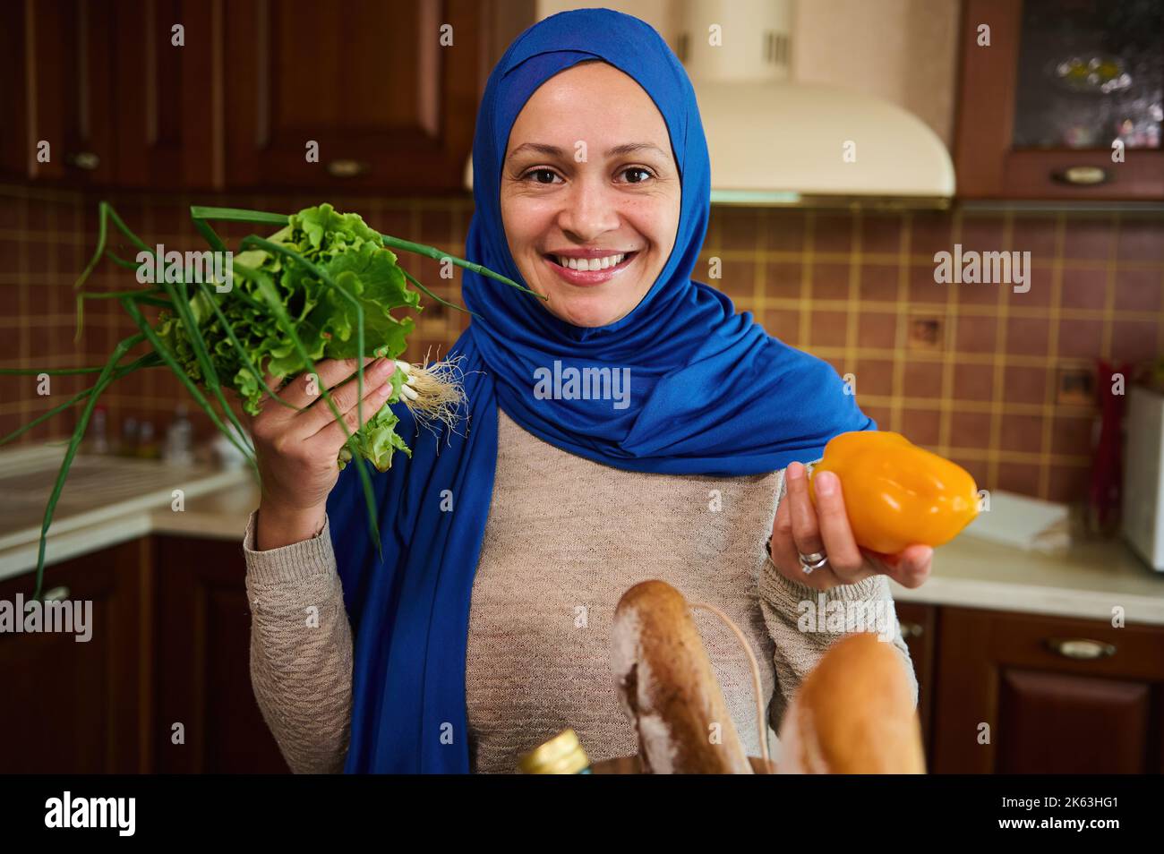 Middle Eastern Muslim woman in blue hijab, holding fresh greens and ...