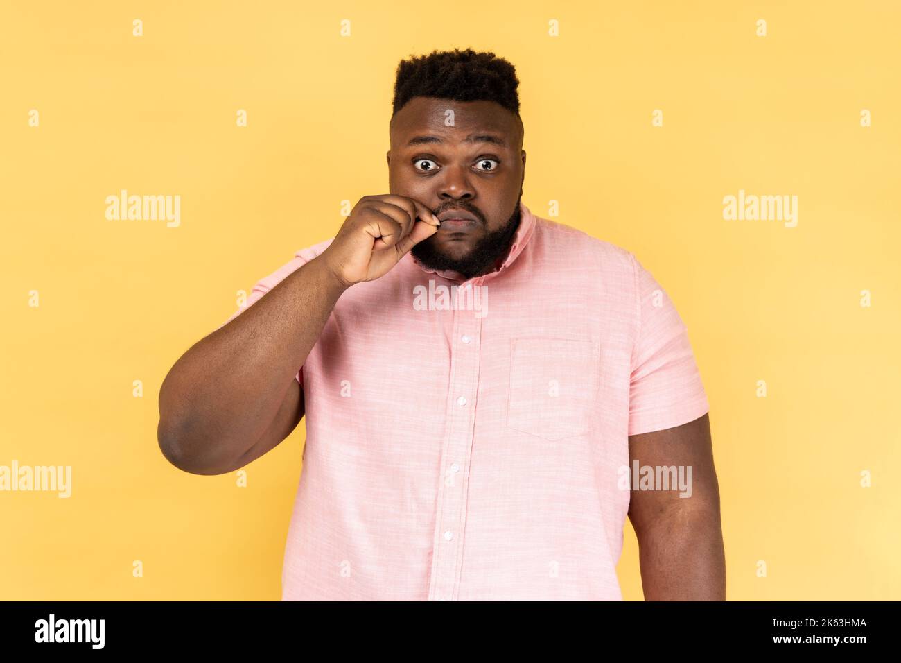 I won't tell anyone. Portrait of intimidated man wearing pink shirt ...