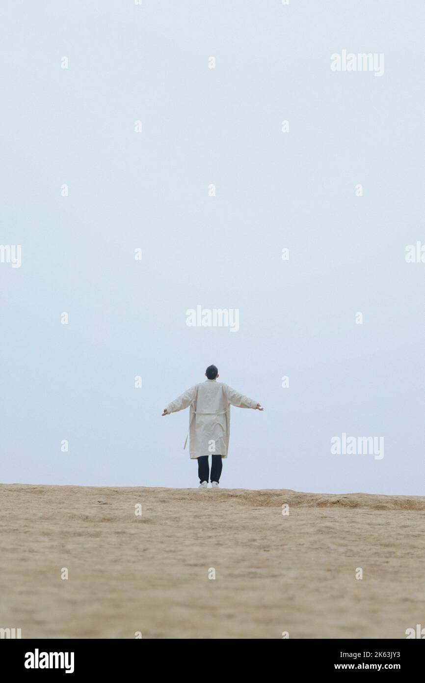 A vertical back view of a person in a white coat standing with spread ...