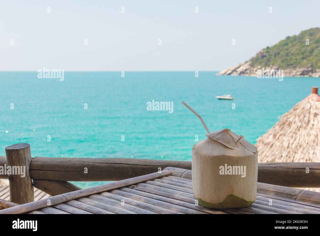 Big coconut with straw on bamboo table overlooking the sea in the ...