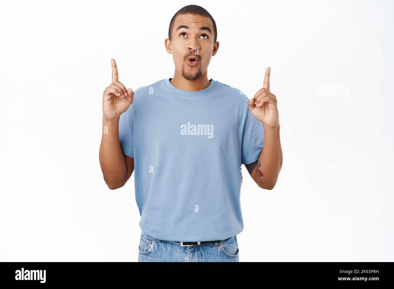 Portrait of surprised man pointing fingers up, looking up on top with ...