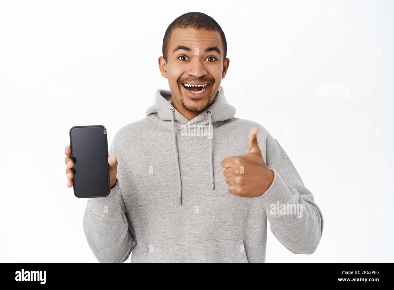 Enthusiastic arab guy shows mobile phone screen and thumbs up ...