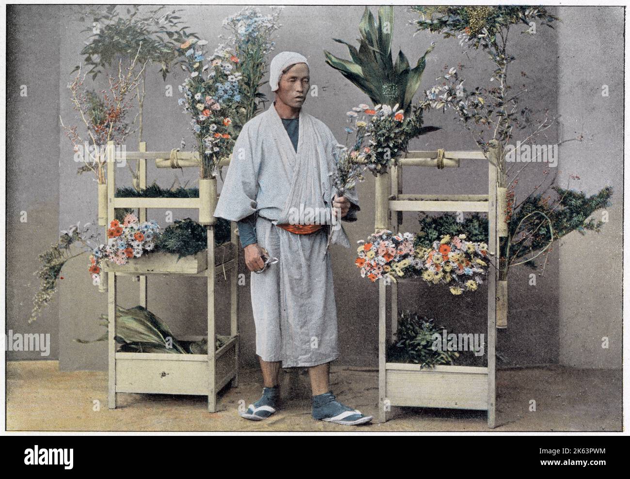 A Japanese flower seller stands by a portable stall made of bamboo with ...