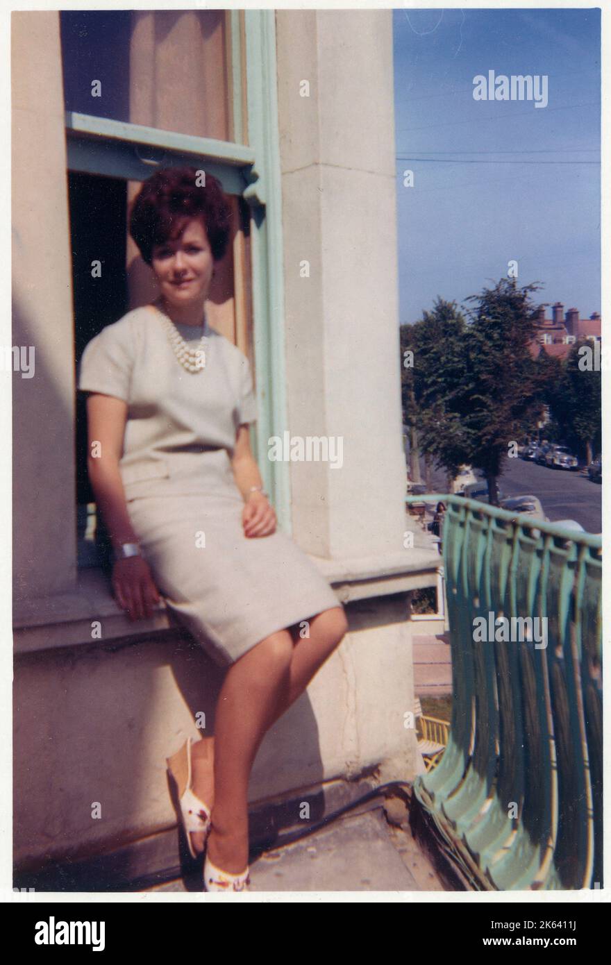 A young lady in a pale dress seated on the outer window ledge of a ...
