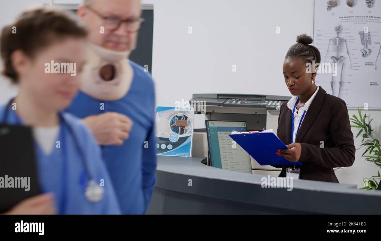 African american receptionist helping patient with neck collar at ...