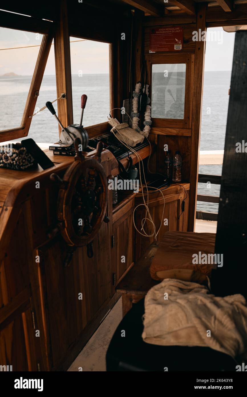 A vertical shot of a wooden boat interior with the wheel and windows ...