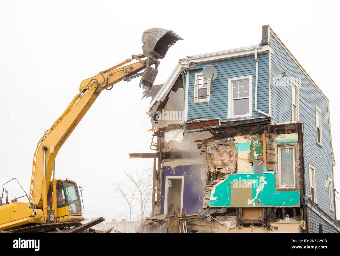 Demolishing a building with a large backhoe. Overcast day. Air is dusty ...