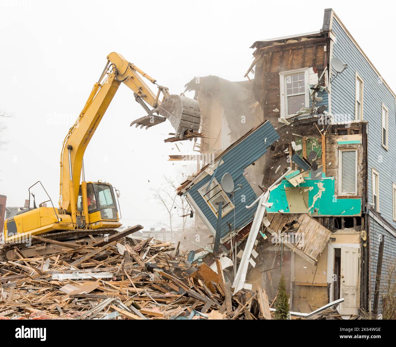 Demolishing a building with a large backhoe. Overcast day. Air is dusty ...
