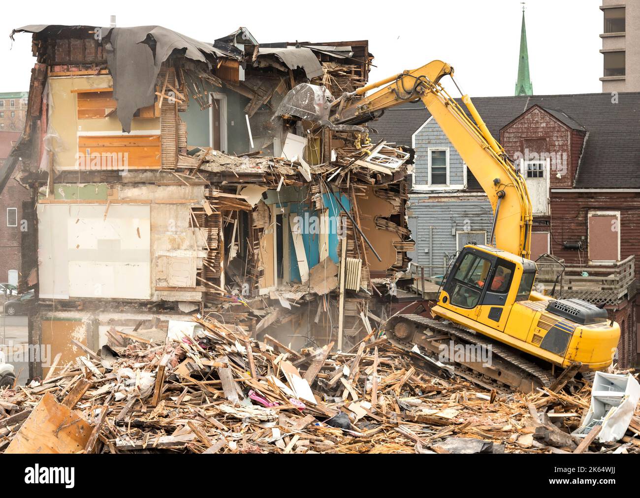 Demolishing a building with a large backhoe. Overcast day. Air is dusty ...