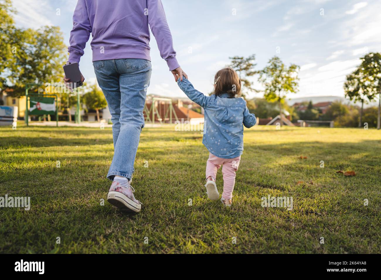 back view of unknown mother and child woman and daughter female girl walking in park while ...