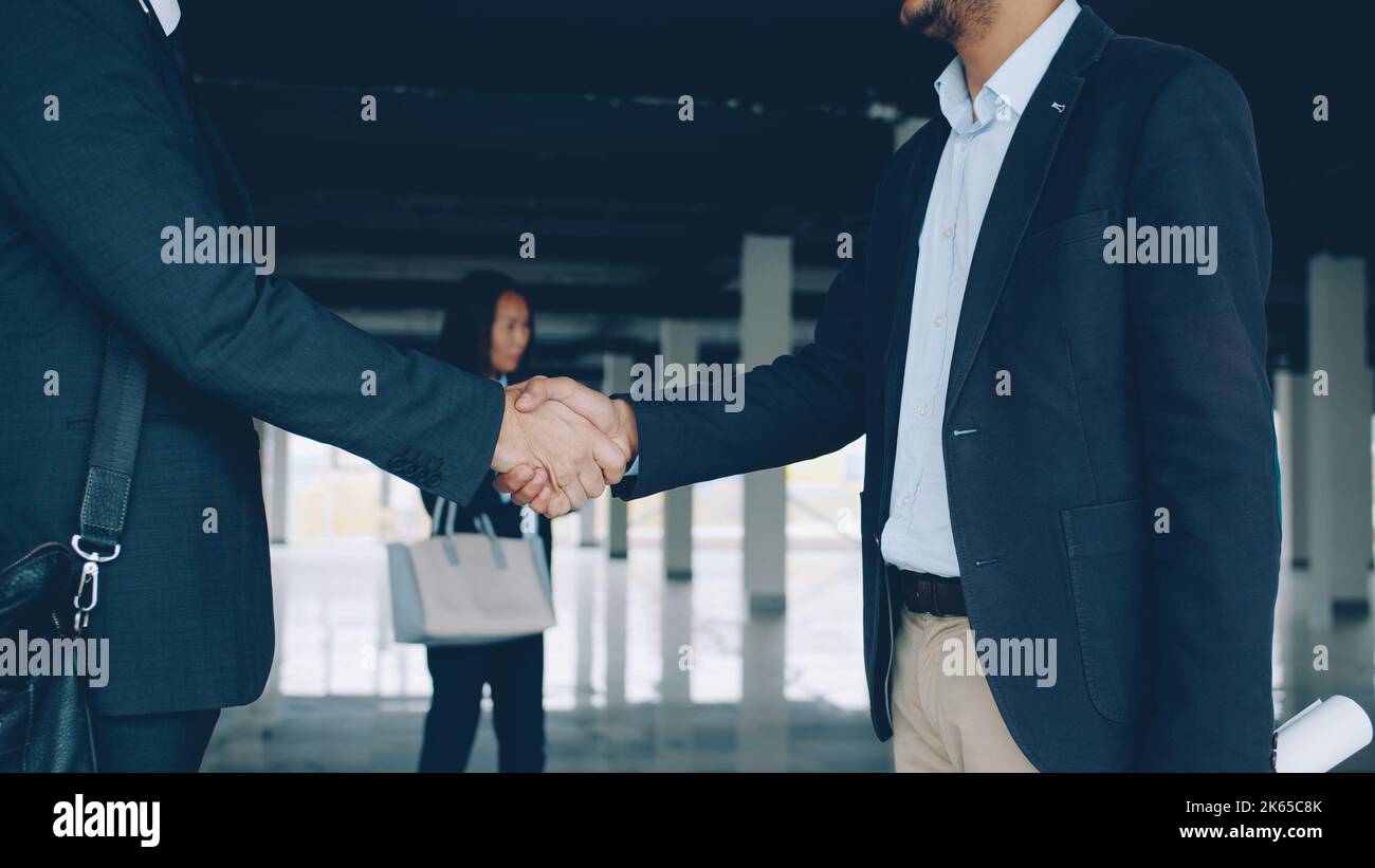 close-up of men shaking hands inside spacious industrial building after ...