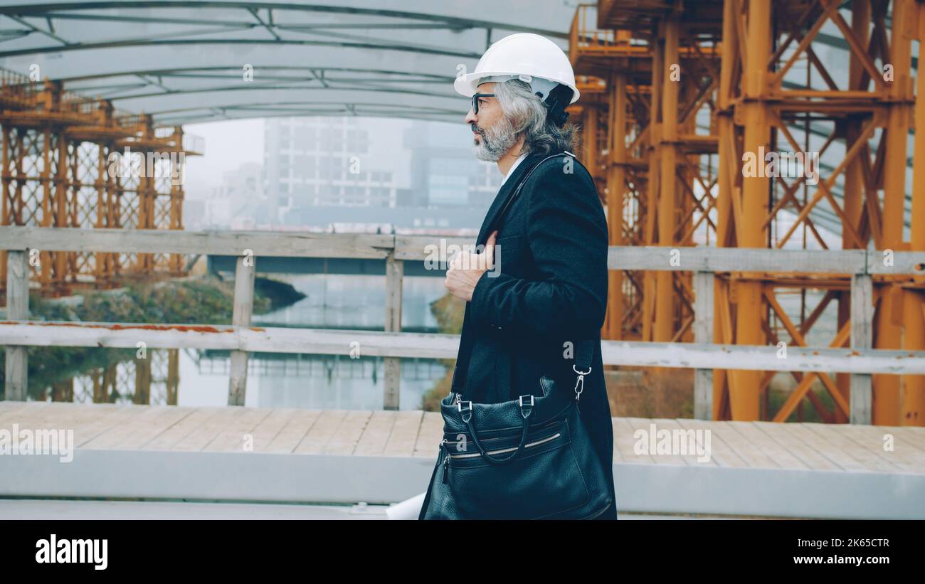 Confident mature man investor is working in construction site holding blueprint . People and ...