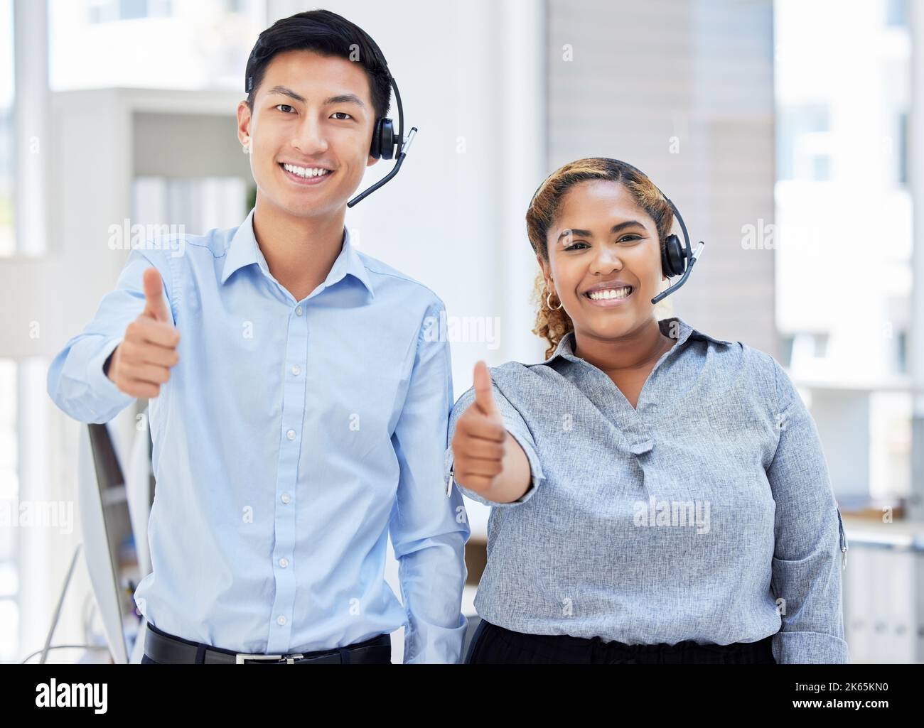 Two young positive male and female call center agents showing thumbs up ...