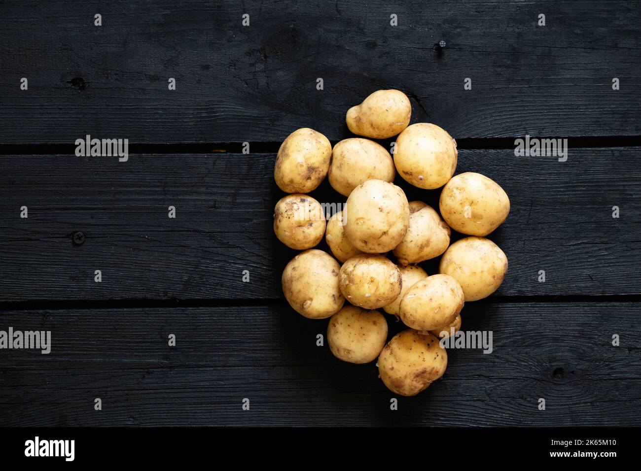 young raw potatoes lie on a black wooden table, potatoes on a wooden ...