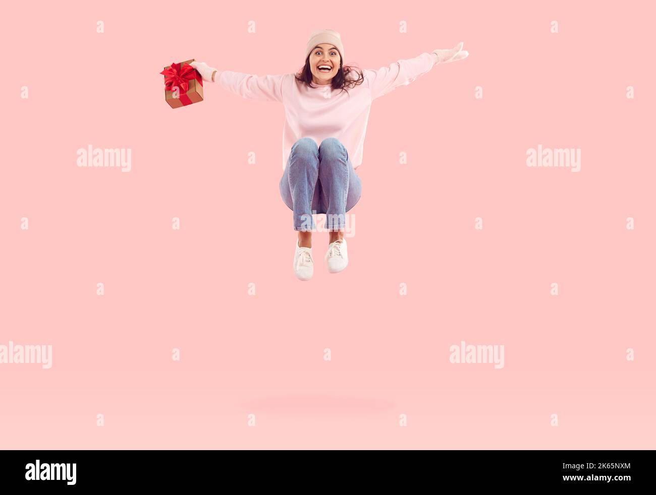 Joyful excited woman with Christmas present jumping high in air on pink ...