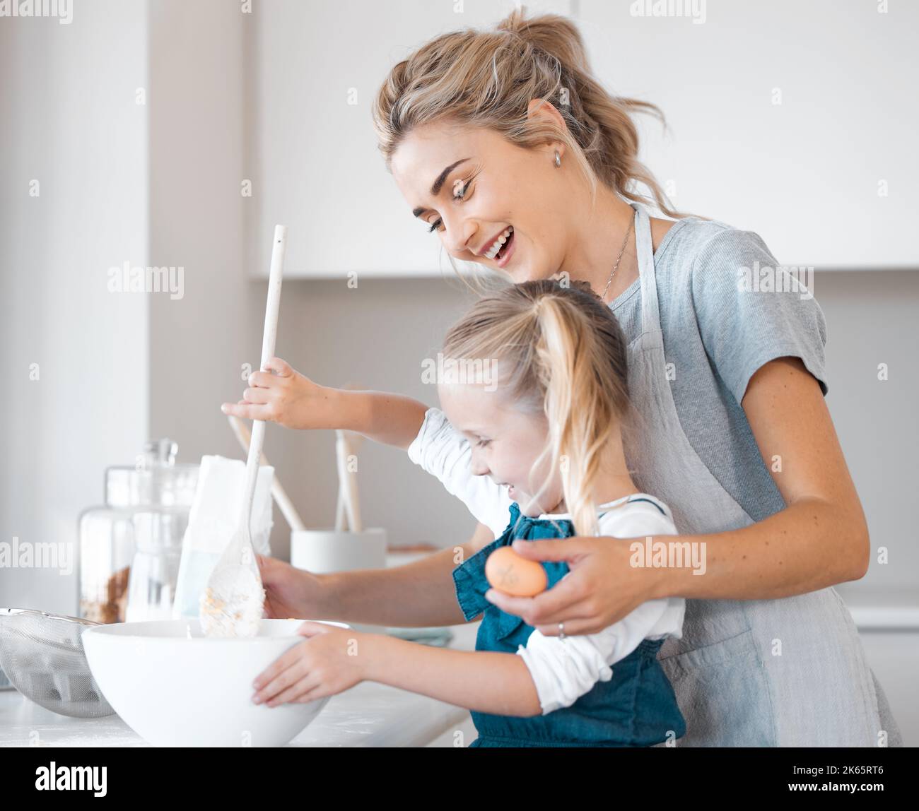 Mother helping her daughter bake. Happy woman holding an egg helping ...