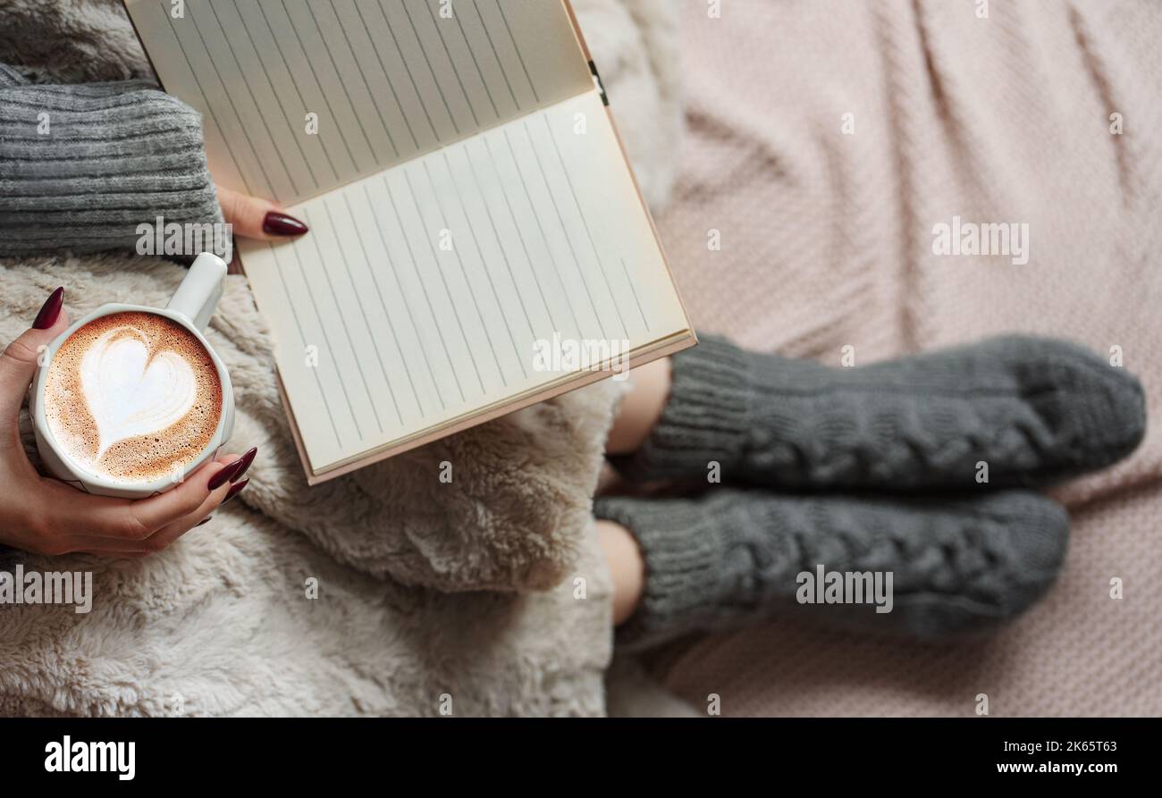 Cozy home, woman covered with warm blanket, drinks coffee and reeds the ...