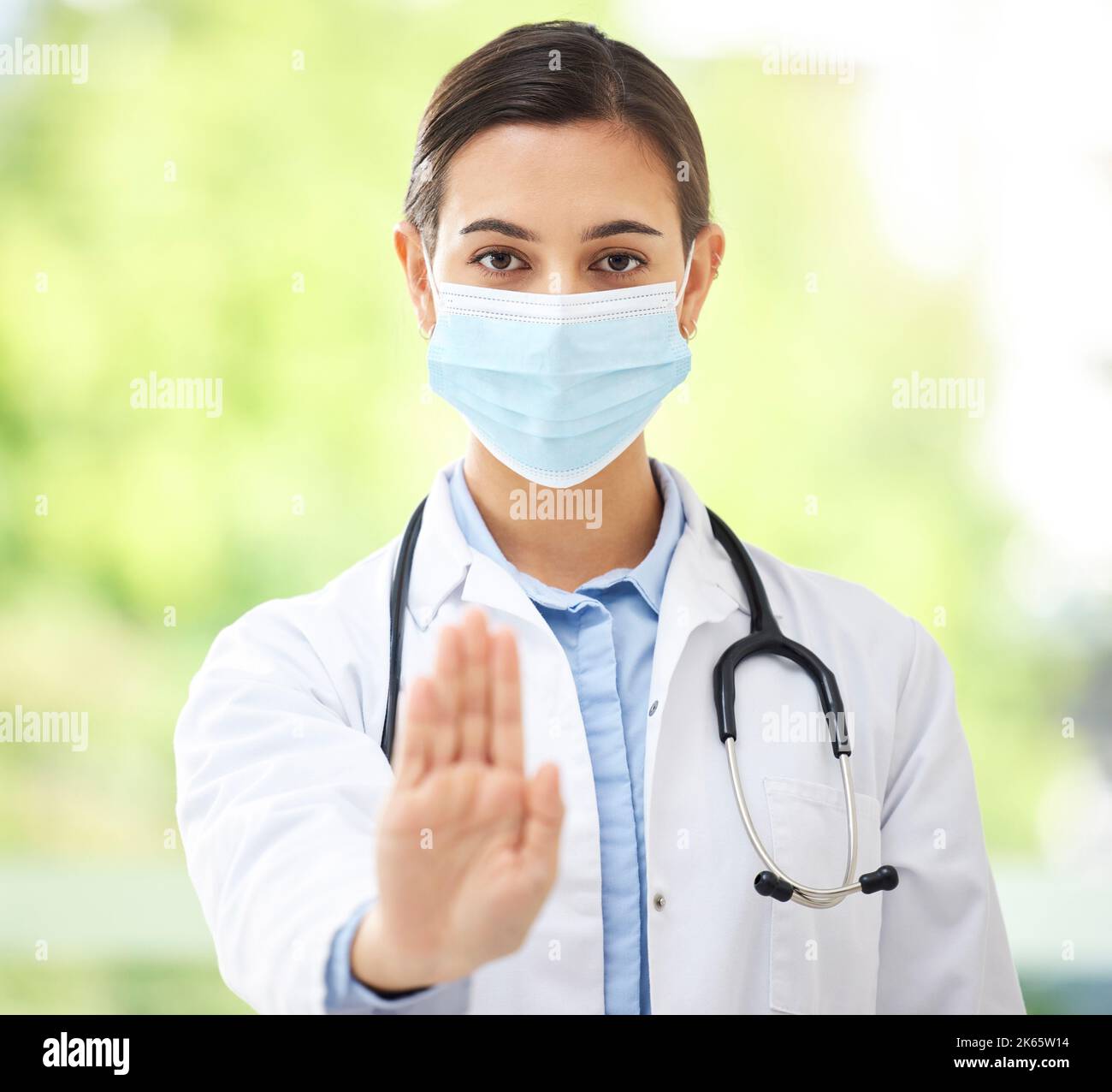 Portrait of a hispanic female doctor wearing a mask and showing a stop ...