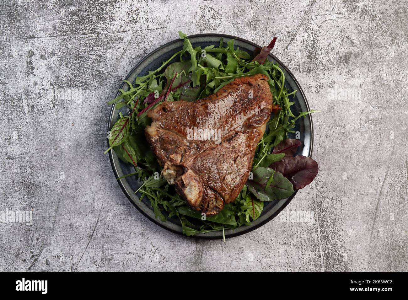 Roast T-bone steak and herbs on a round plate on a dark gray background ...