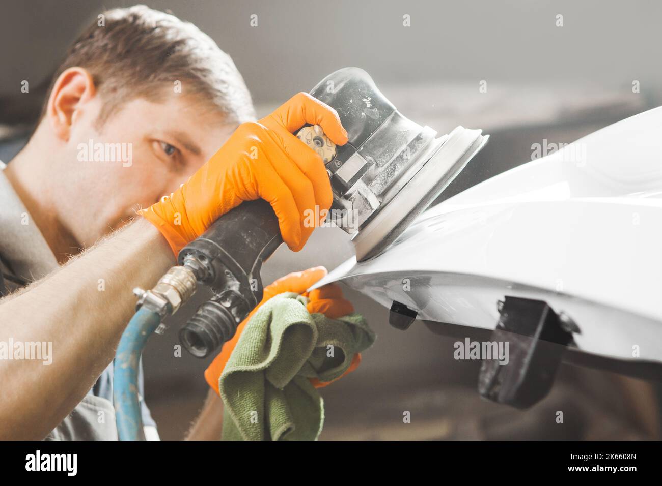 Auto mechanic grinds white car part after painting before polishing ...