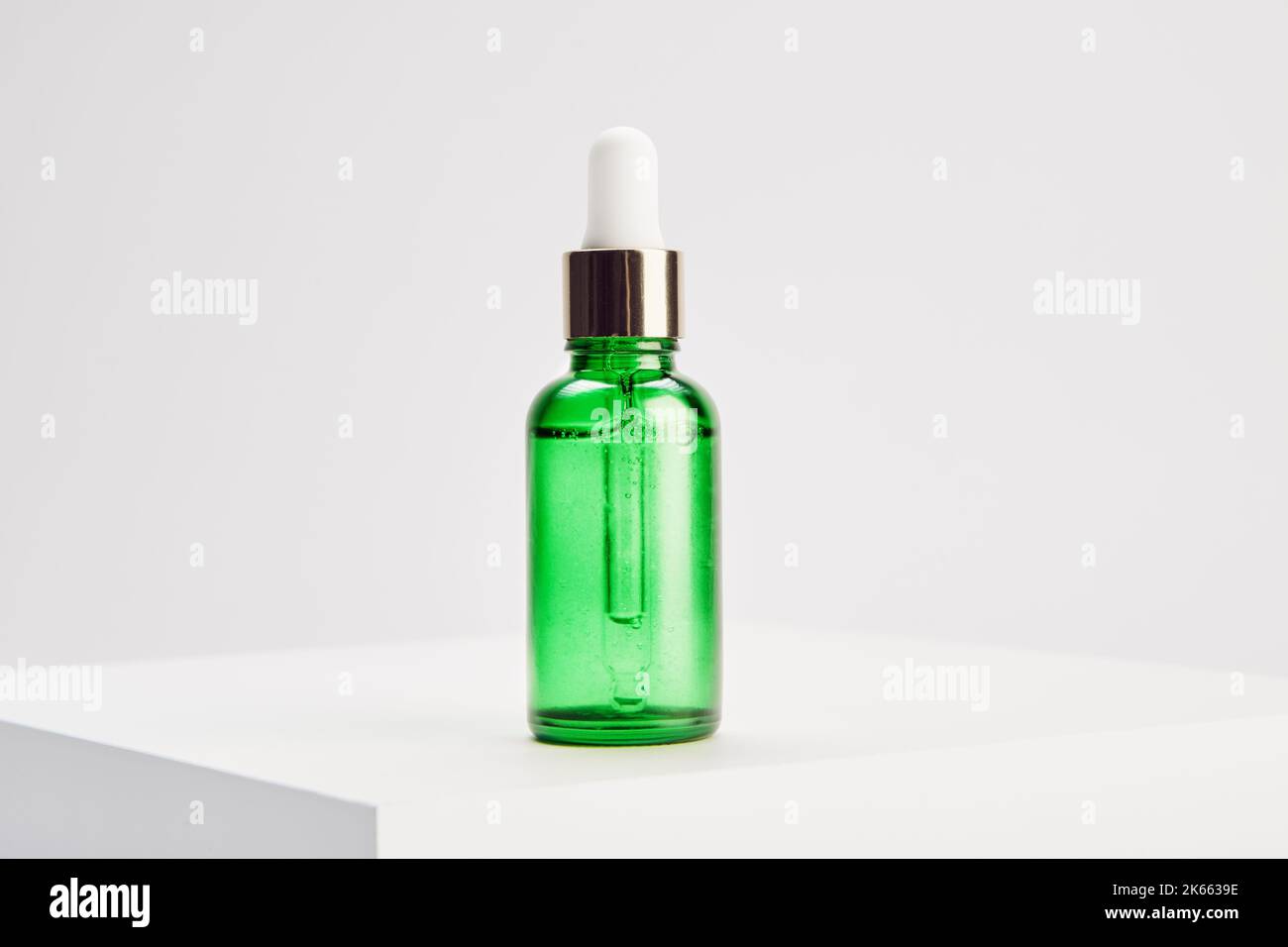 Green glass vial with gold dropper cap is on platform Stock Photo - Alamy