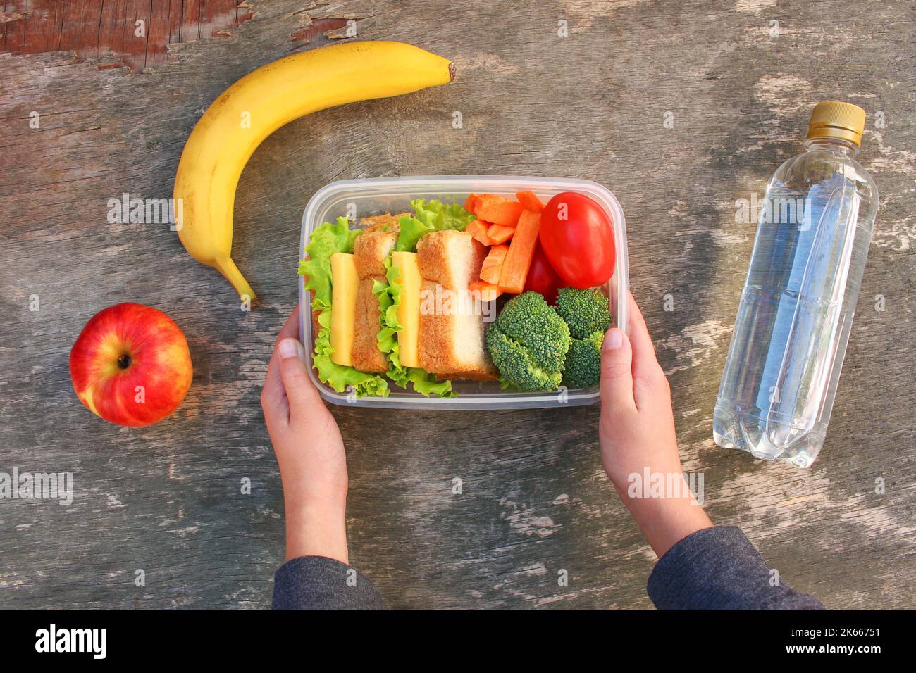 Sandwiches, fruits and vegetables in food box, water on old wooden ...