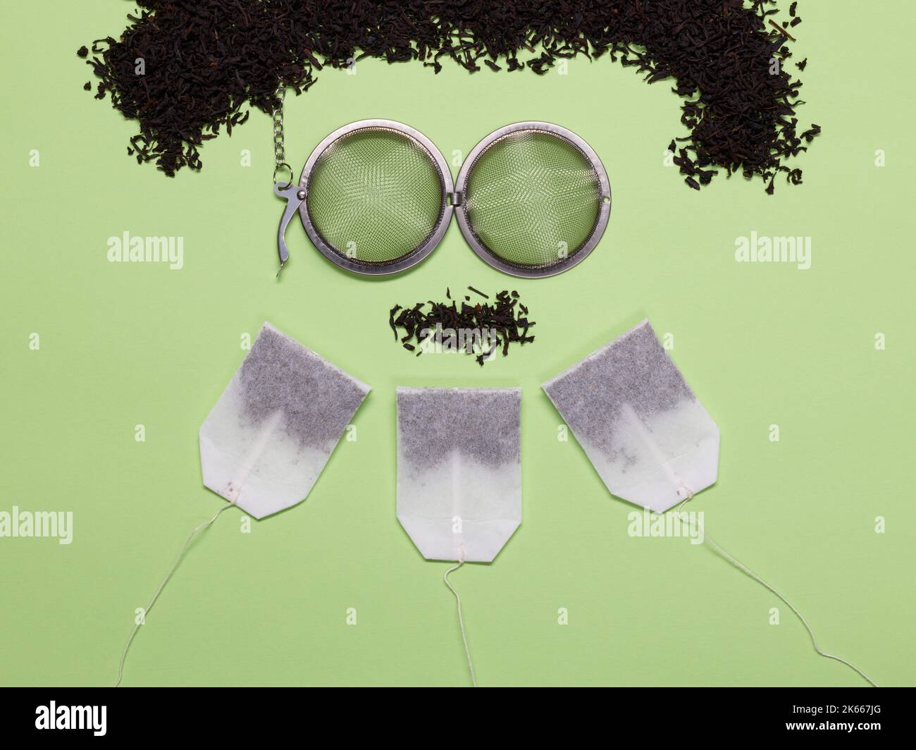 Three green tea bags, metal tea filter and heap of black tea on green ...