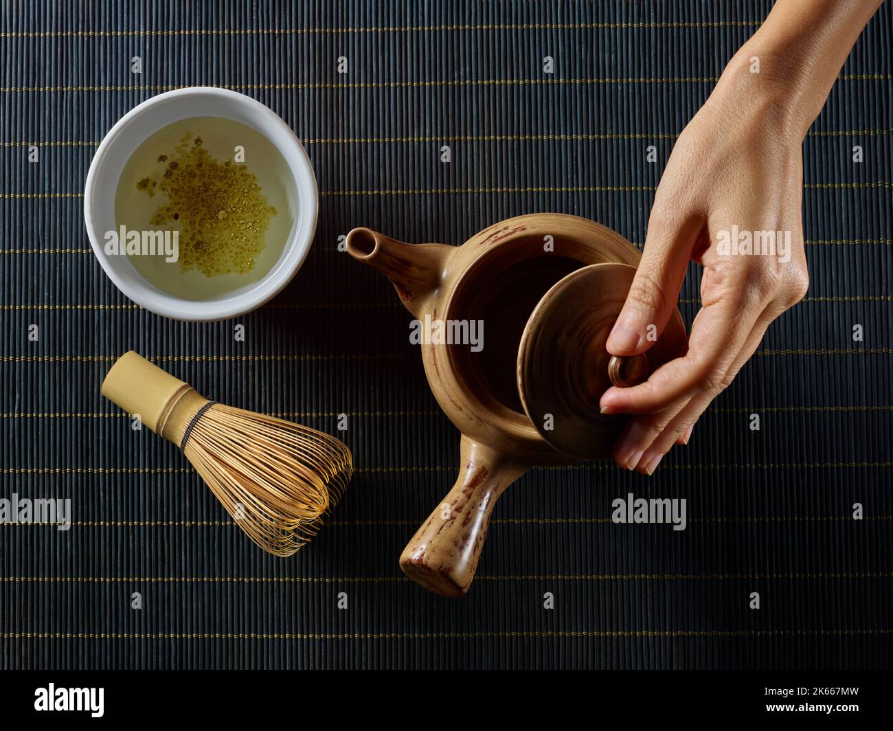 Hand lifting the lid of a teapot, next to a cup with matcha tea Stock ...
