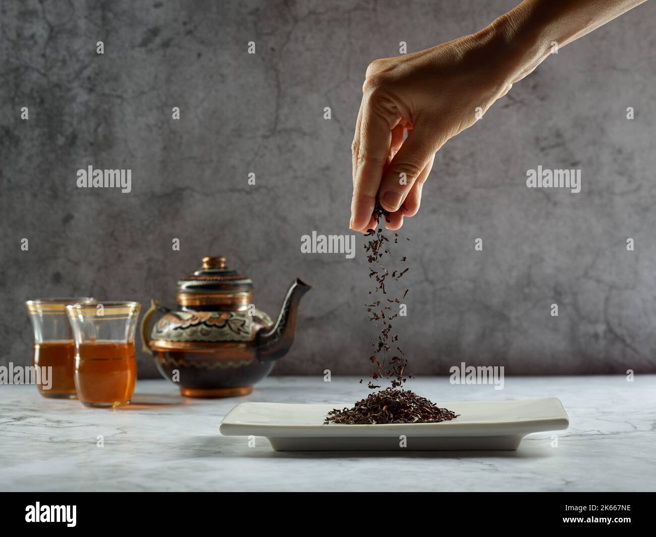 Hand dropping black tea onto a tray, with a metal teapot and two glass ...