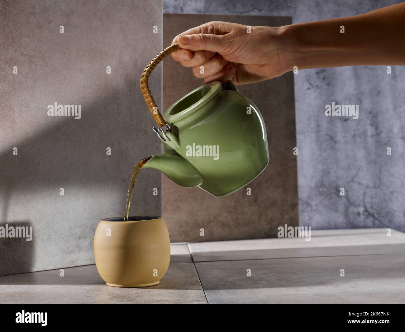 Hand picking up a green teapot, pouring tea into a cup Stock Photo - Alamy