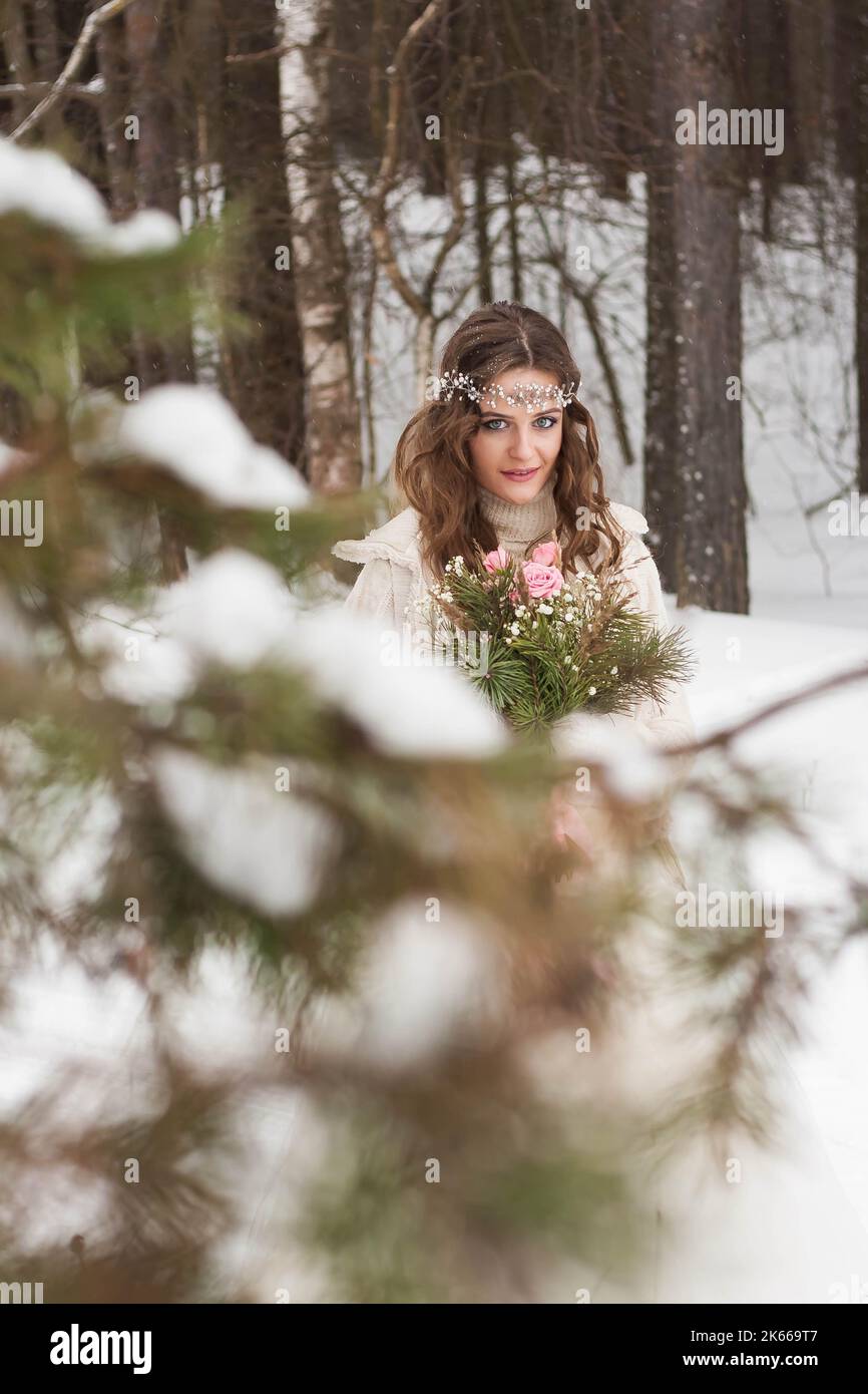 Beautiful bride in a white dress with a bouquet in a snow-covered ...