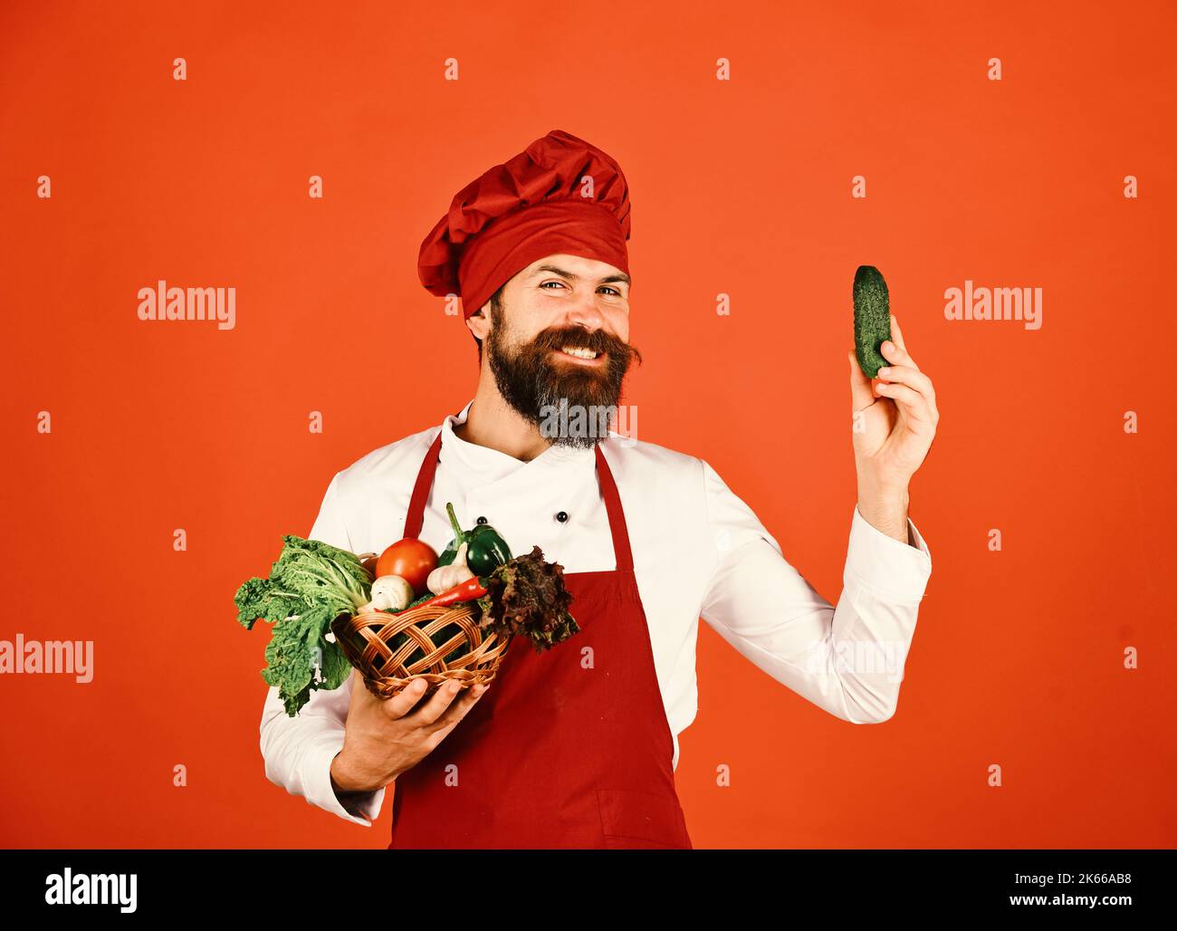 Cook with smile in burgundy uniform holds cucumber Stock Photo - Alamy