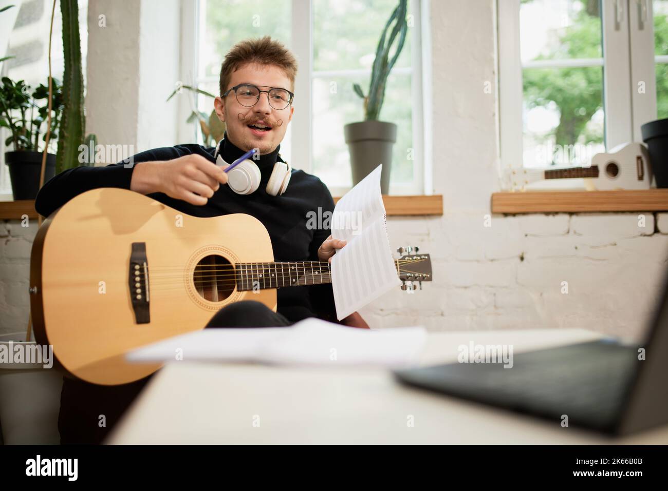 Online music class. Young man siiting on floor at home and leaning to ...