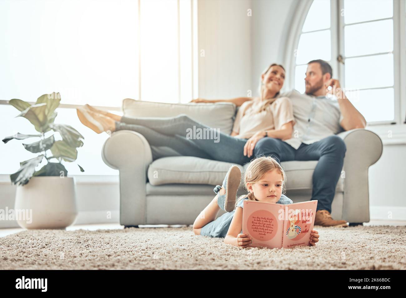 Little girl reading storybook while lying on carpet at home. Smart kid ...