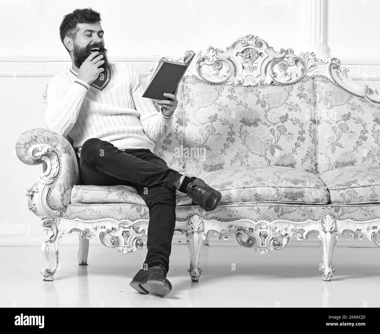 Man with beard and mustache sits on baroque style sofa, holds book ...