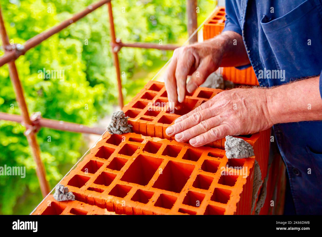 Mason, bricklayer worker is using red blocks to mount a wall next the ...