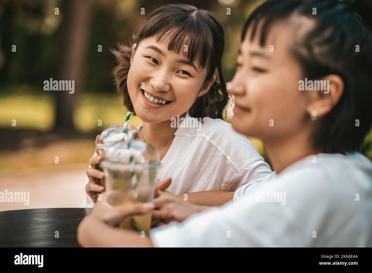 Two asian young girls having good time together and drinking lemonade ...