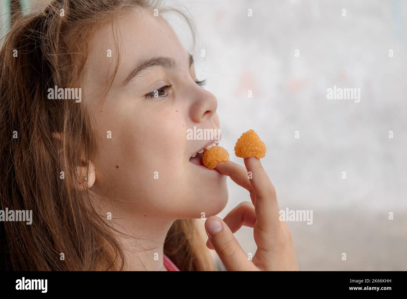 Young girl is holding yellow raspberries on her fingers and tasting ...