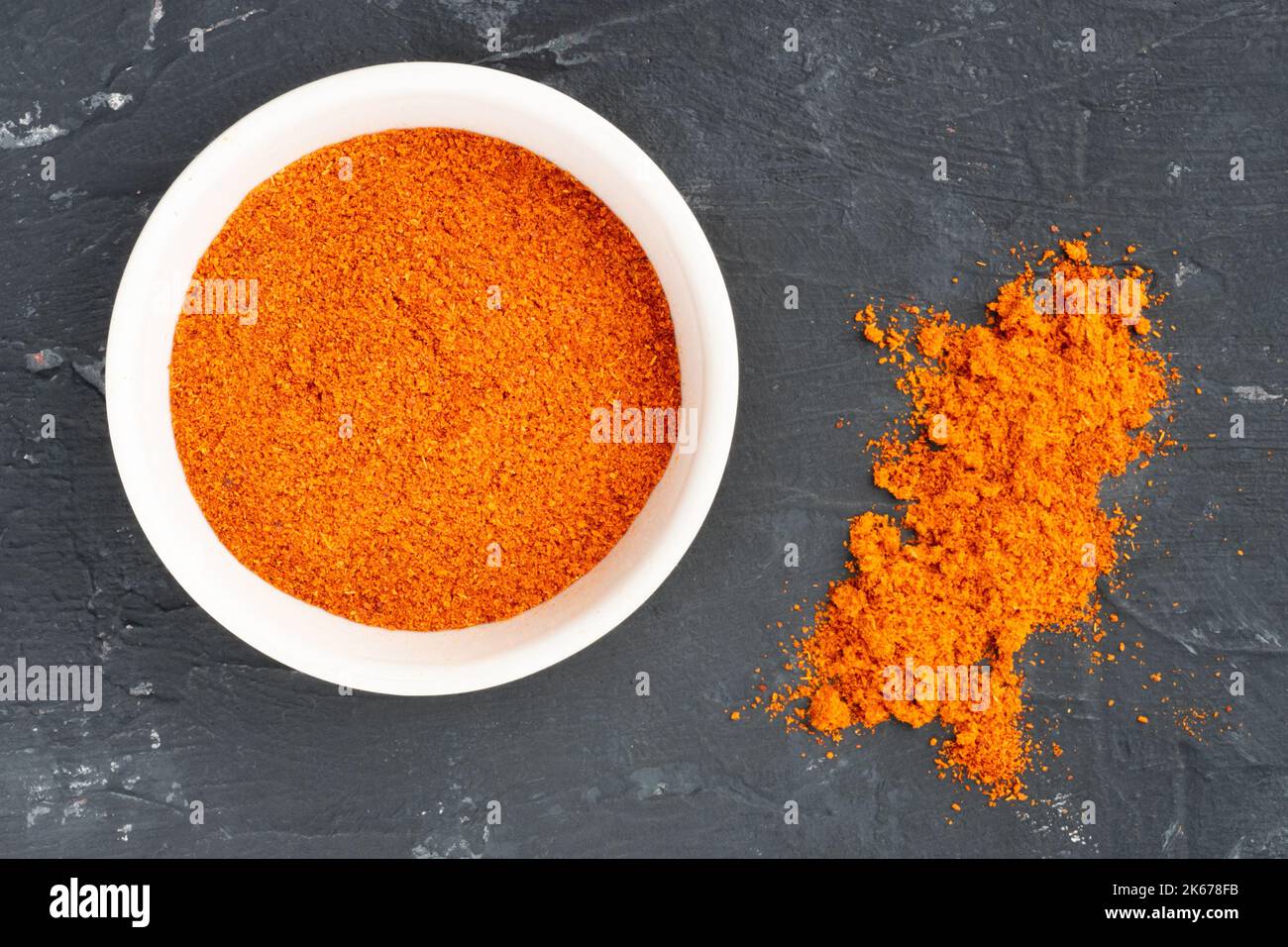 Red chili pepper spice in ceramic bowl and scatter on black concrete ...