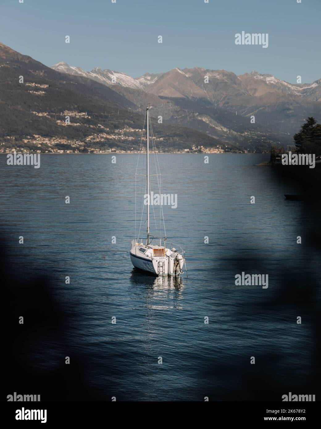 A vertical shot of a boat in a middle of a lake with mountains in the ...
