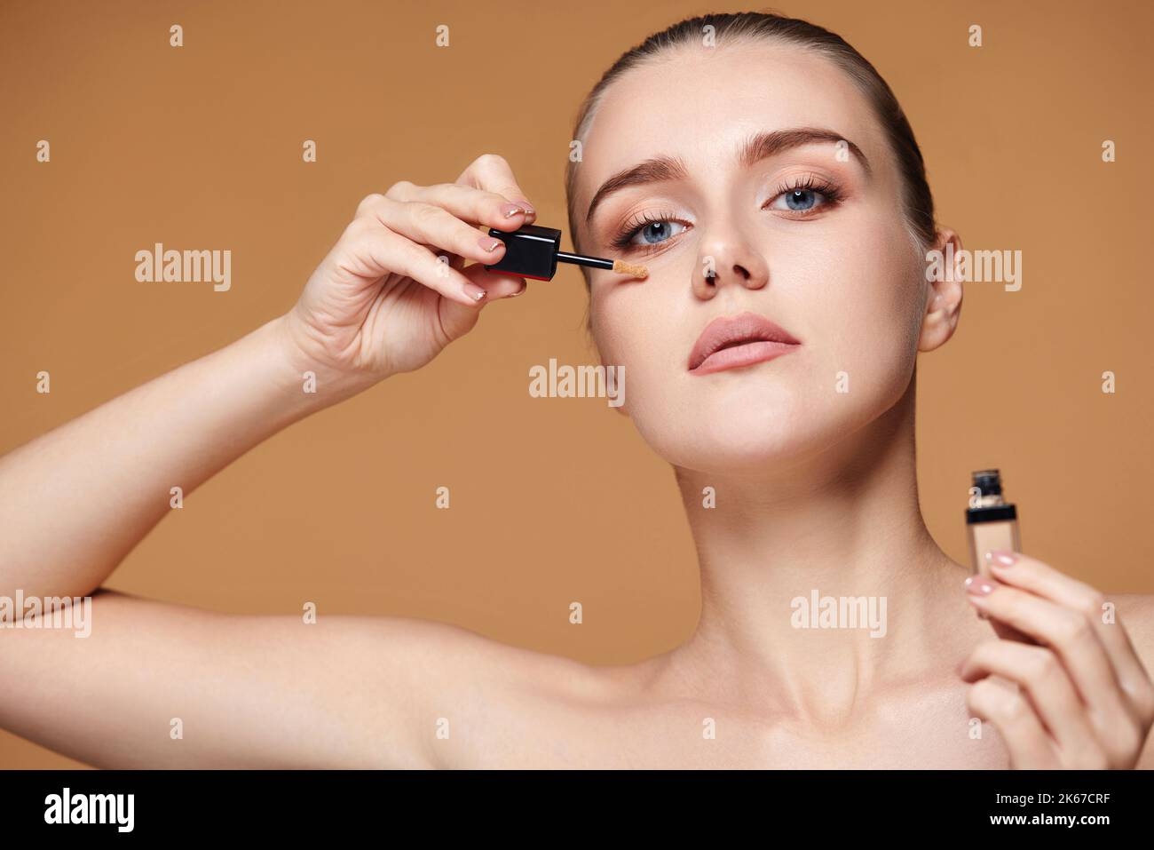 woman applying concealer under her eyes on beige background Stock Photo ...