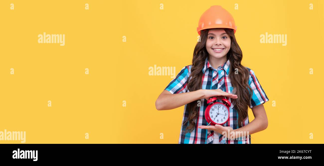 happy child with curly hair in construction helmet showing alarm clock ...