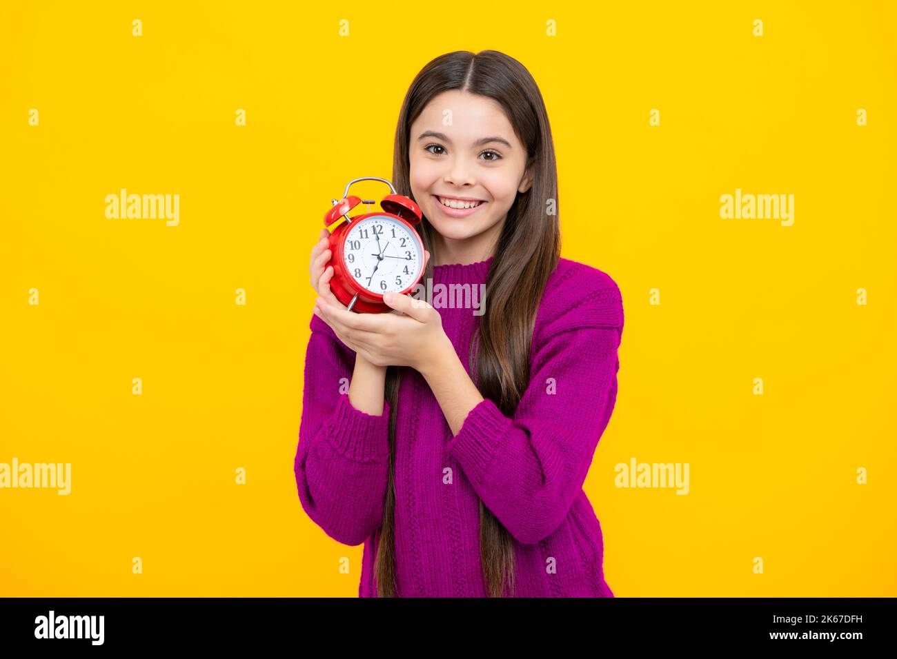 Teen girl holding clock over yellow background. Early morning, daily ...
