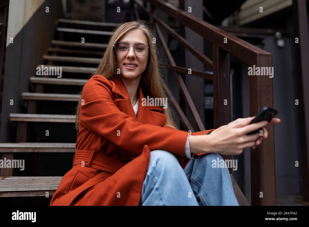 portrait of a stylish young woman with a phone sitting on the steps ...