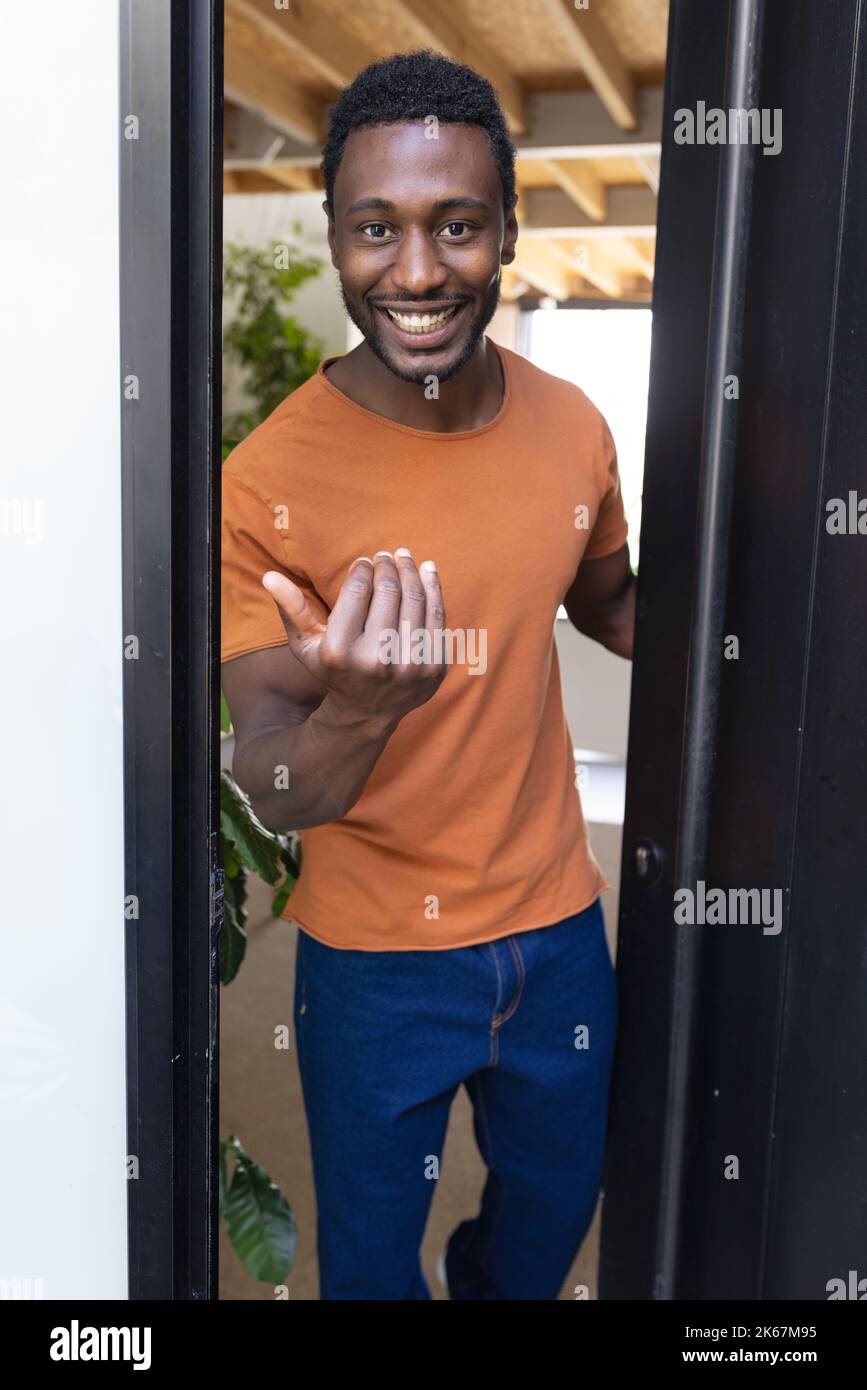 Happy african american man standing in doorway and inviting inside the ...