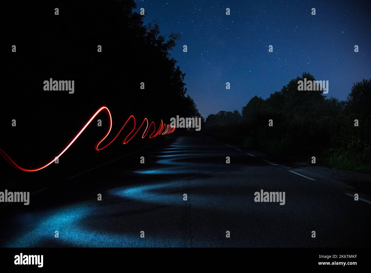 A red light trail in a periodic pattern following a straight road under ...