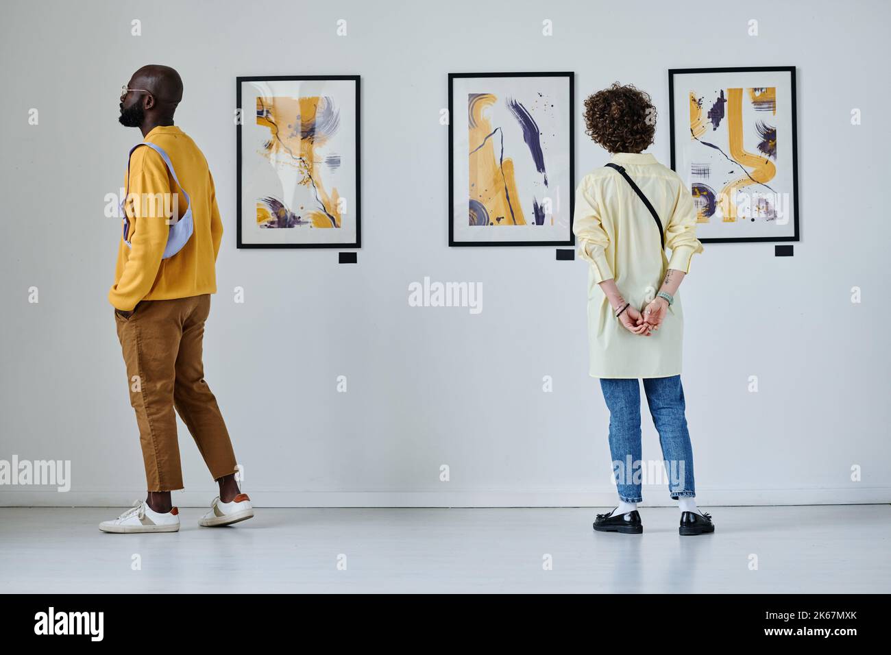 Rear view of young people looking at paintings on the wall at art ...
